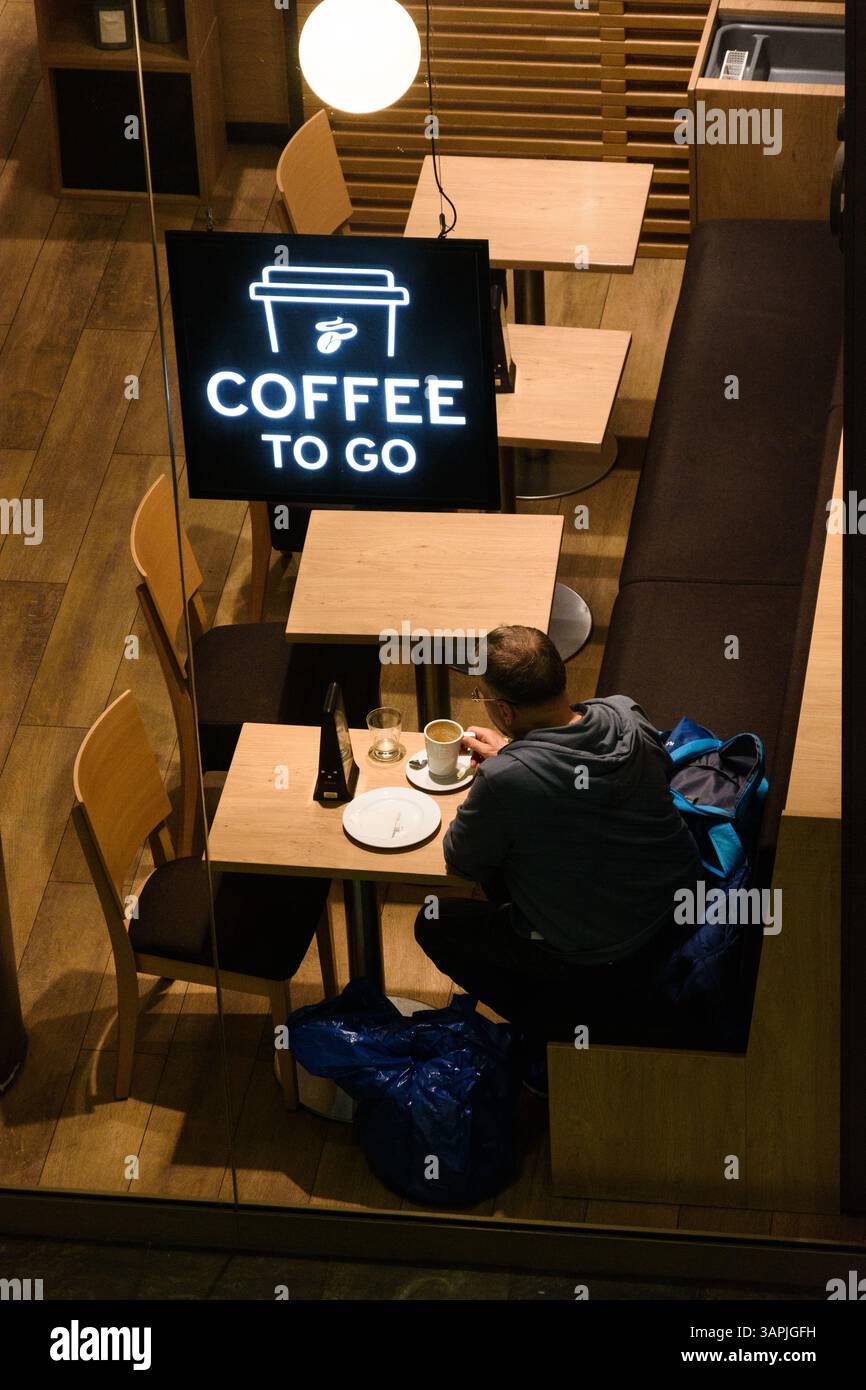 man sitting in a coffeshop drinking coffee, above him a sign "coffee to ...