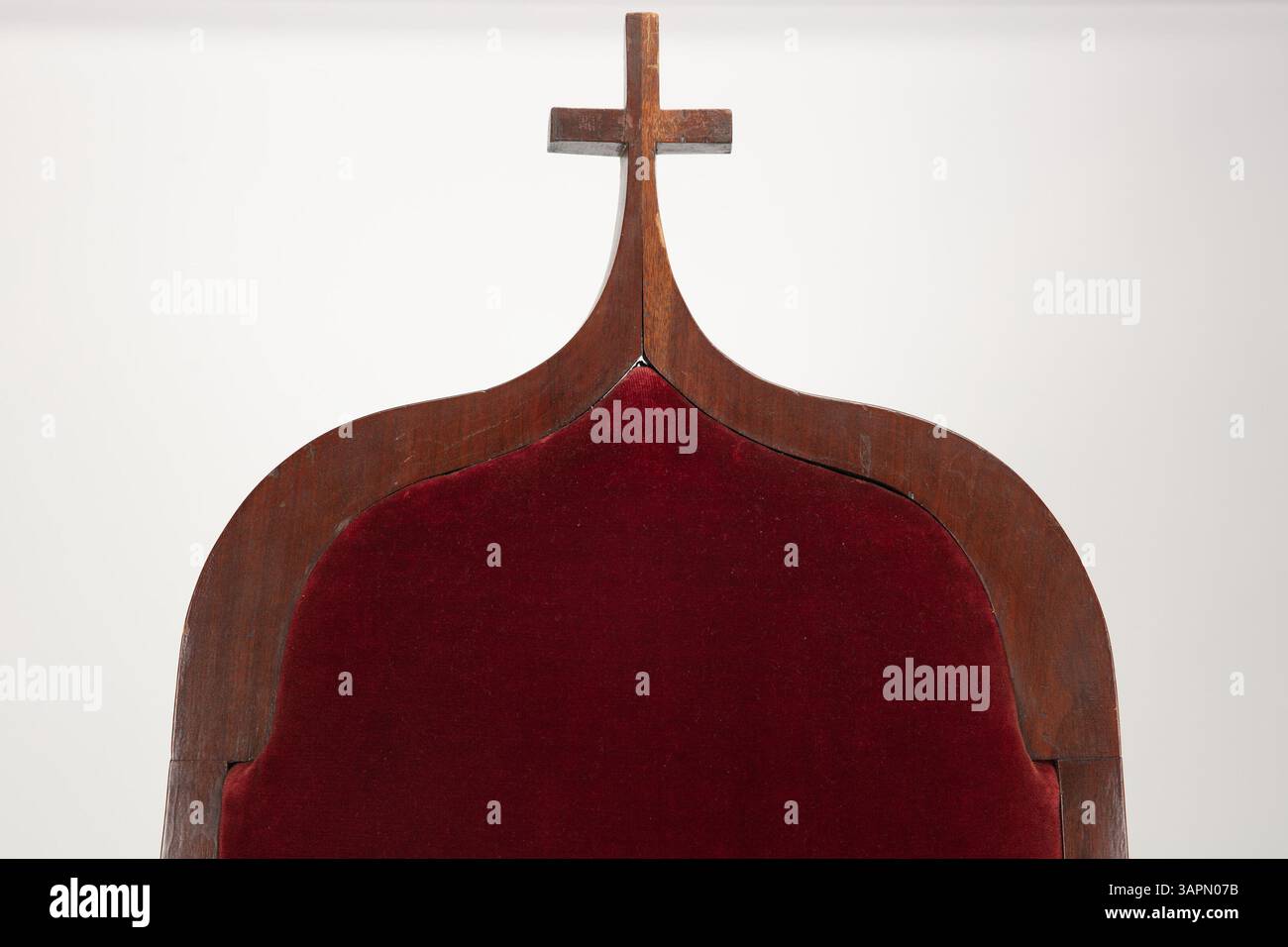 A high-backed priest's chair with a red velvet upholstered seat and ...