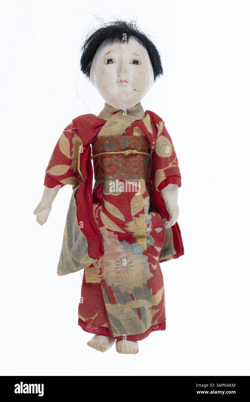 A painted papier mache doll dressed in a red kimono, a traditional ...