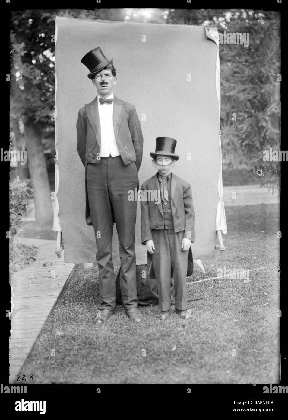 This photograph shows a tall and short man in costume, with a dog ...