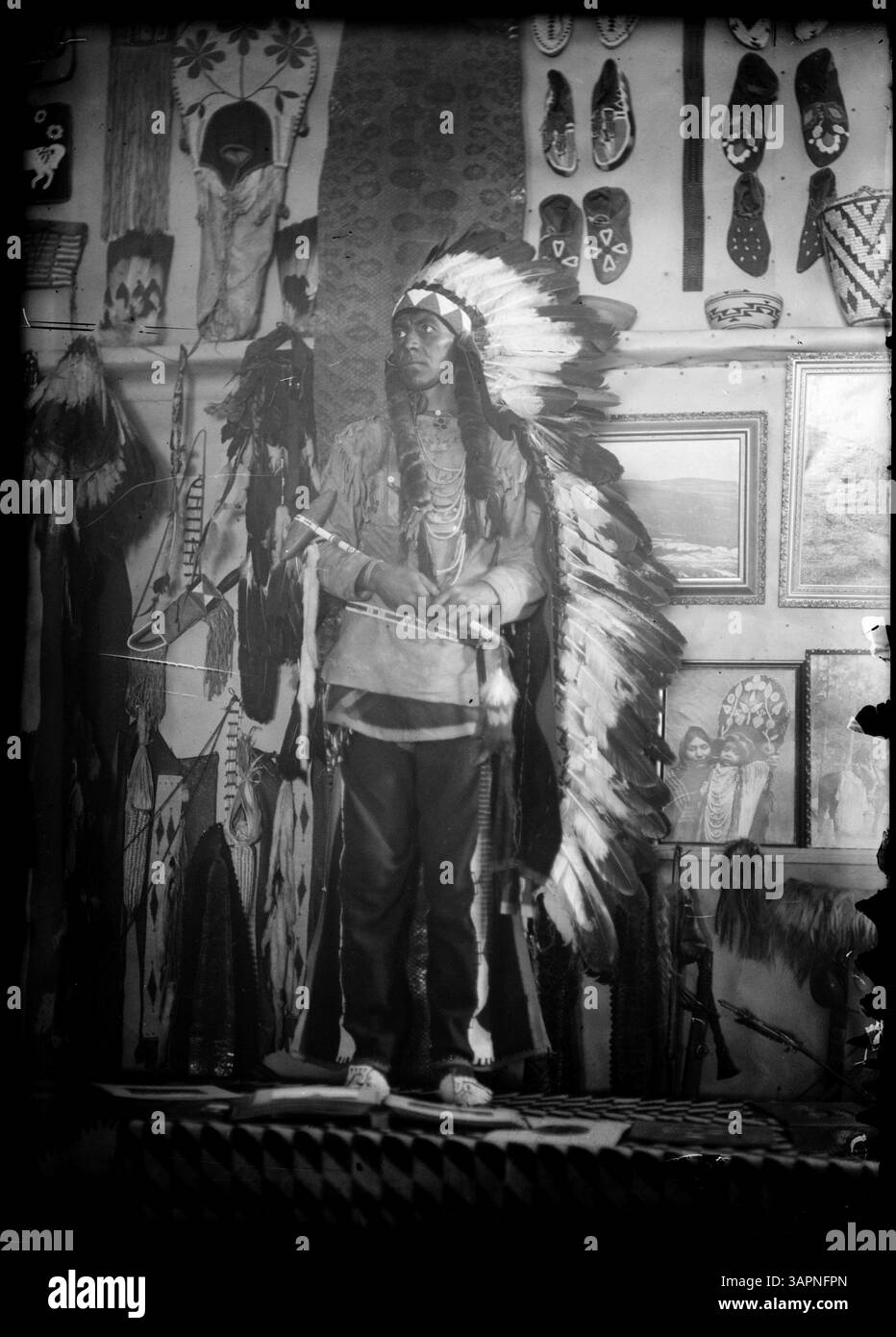 A tribal man is pictured wearing a full-length war bonnet and holding a ...