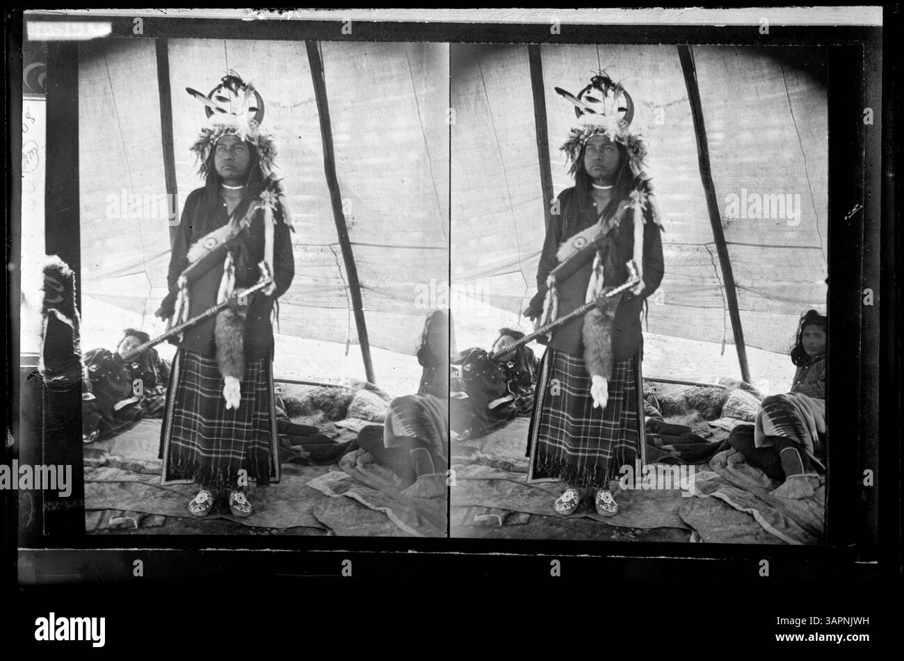 Photograph of Paul Showaway, a tribal man, standing in a canvas tipi ...