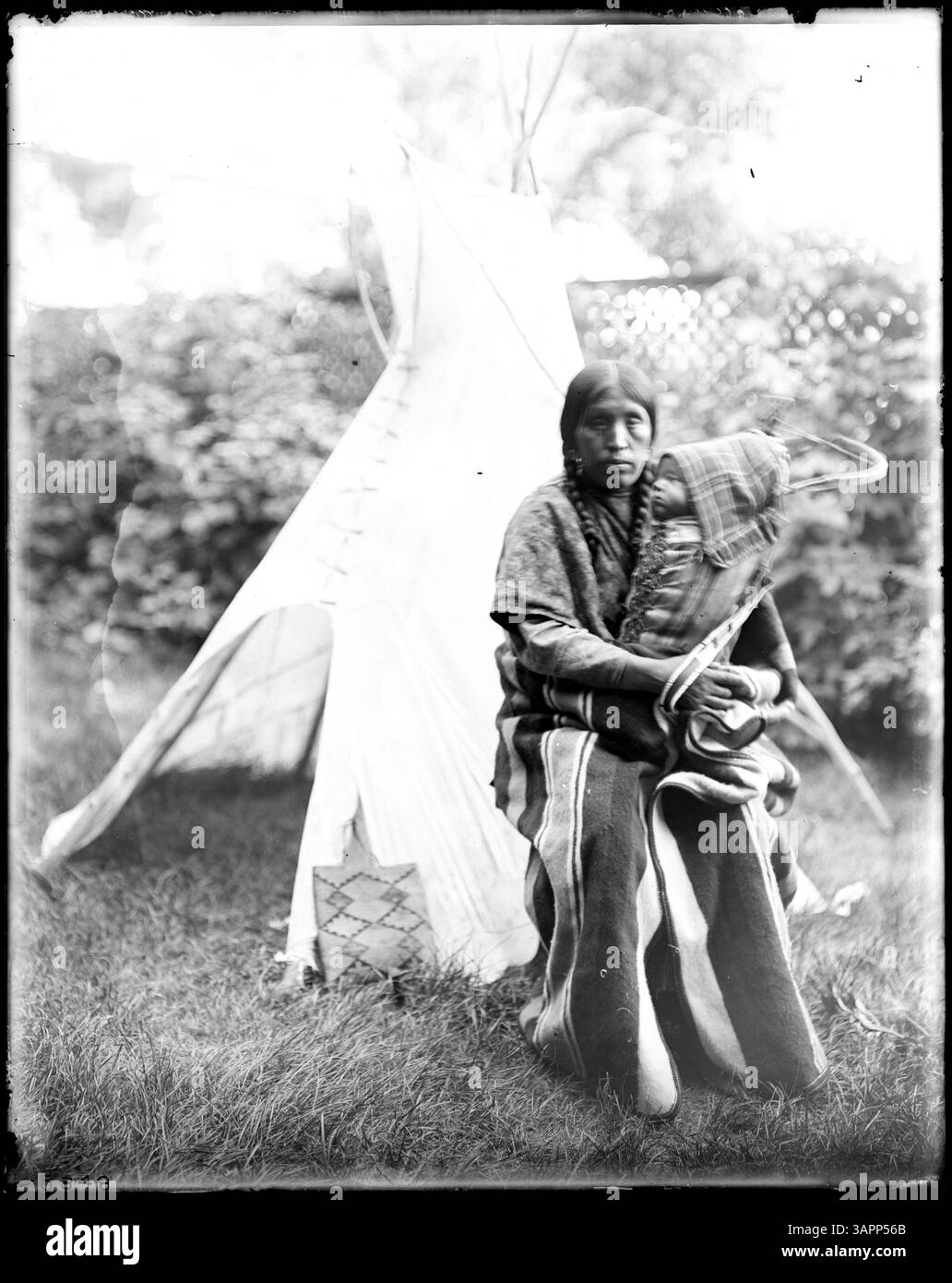 The image captures a tribal woman with an infant in a cradle ...