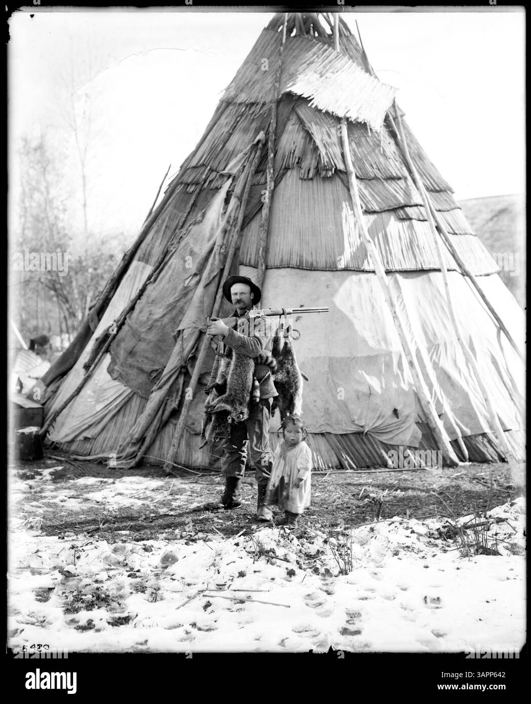 This photograph shows a hunter standing outside a Native American tipi ...