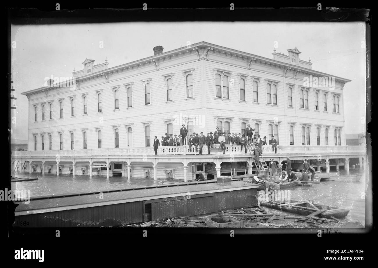 This photograph shows a large white building, dated 1879, with a group ...