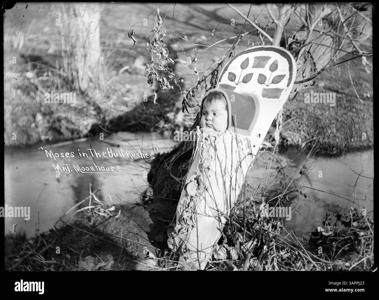 This image depicts a tribal child in a cradleboard by a stream ...
