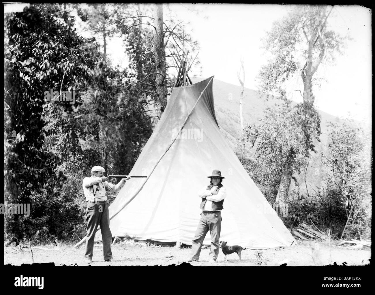 Photograph of two men, a dog, and a tipi, with one man pointing a gun ...