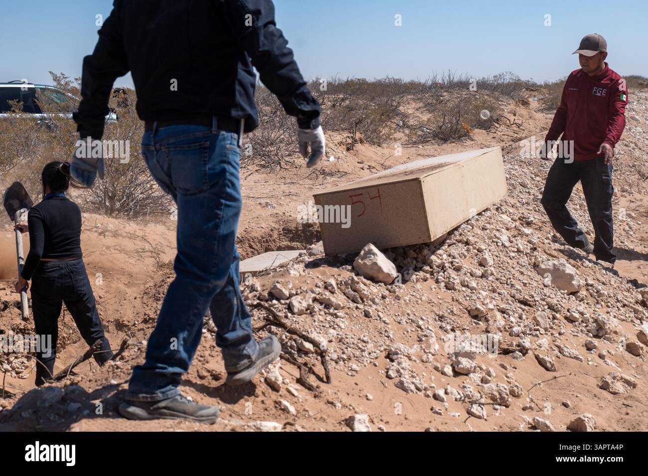 A worker prepares lifting straps to lower a coffin into one of the mass ...