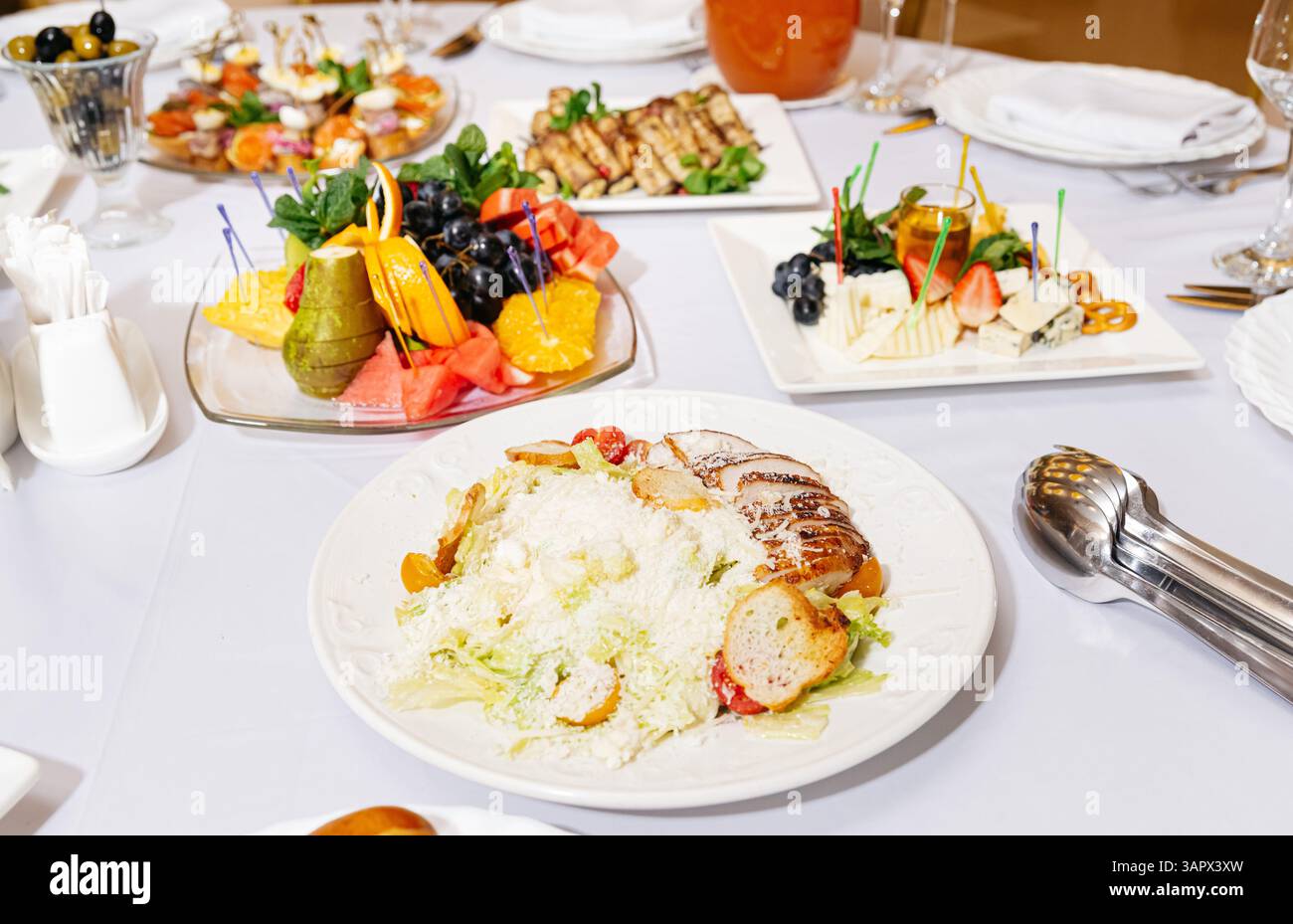 A beautifully set banquet table featuring Caesar salad, grilled meats ...