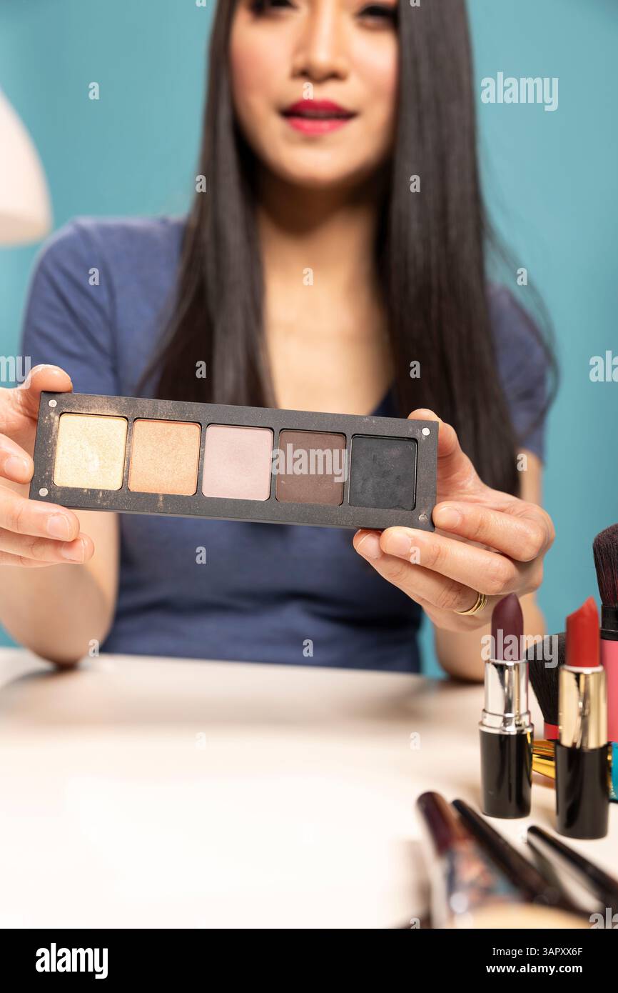 Young asian woman holding a cosmetic product up close, presenting it to ...