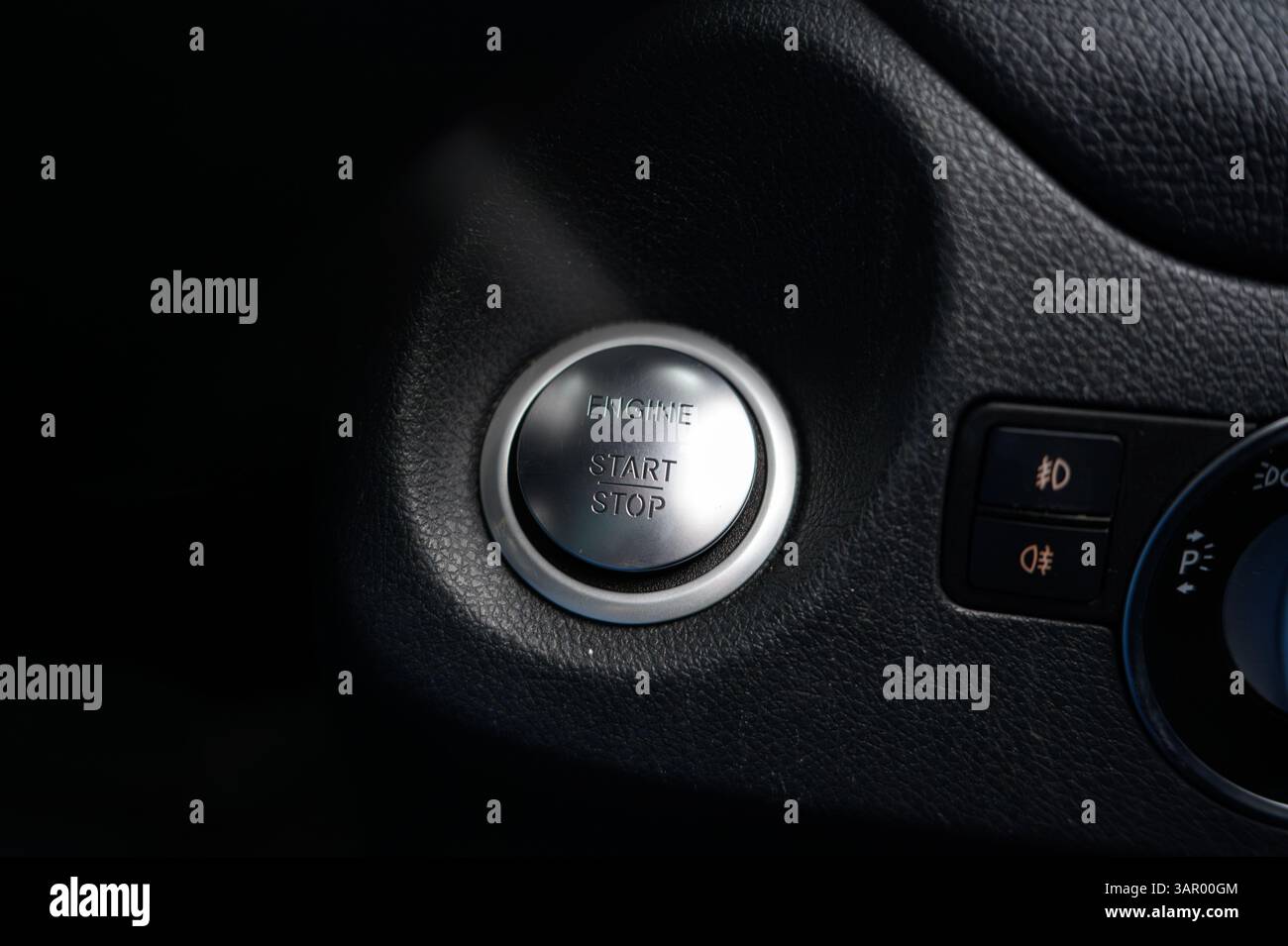 A car's start button is shown in a close up. The button is silver and ...