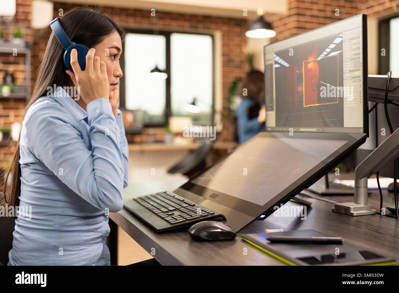 Female designer puts on her headphones and works on digital monitors ...