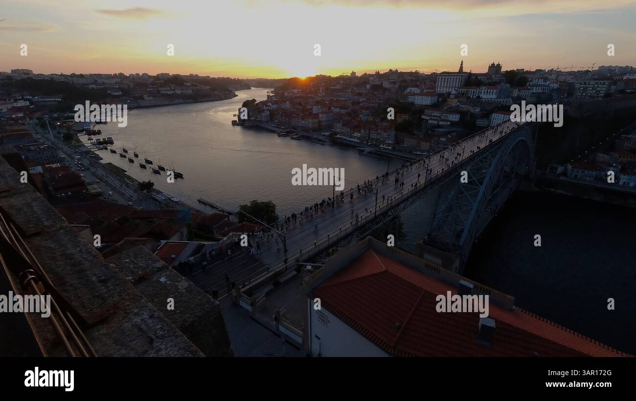 The sun sets over the iconic Dom Luís I Bridge in Porto, casting golden ...
