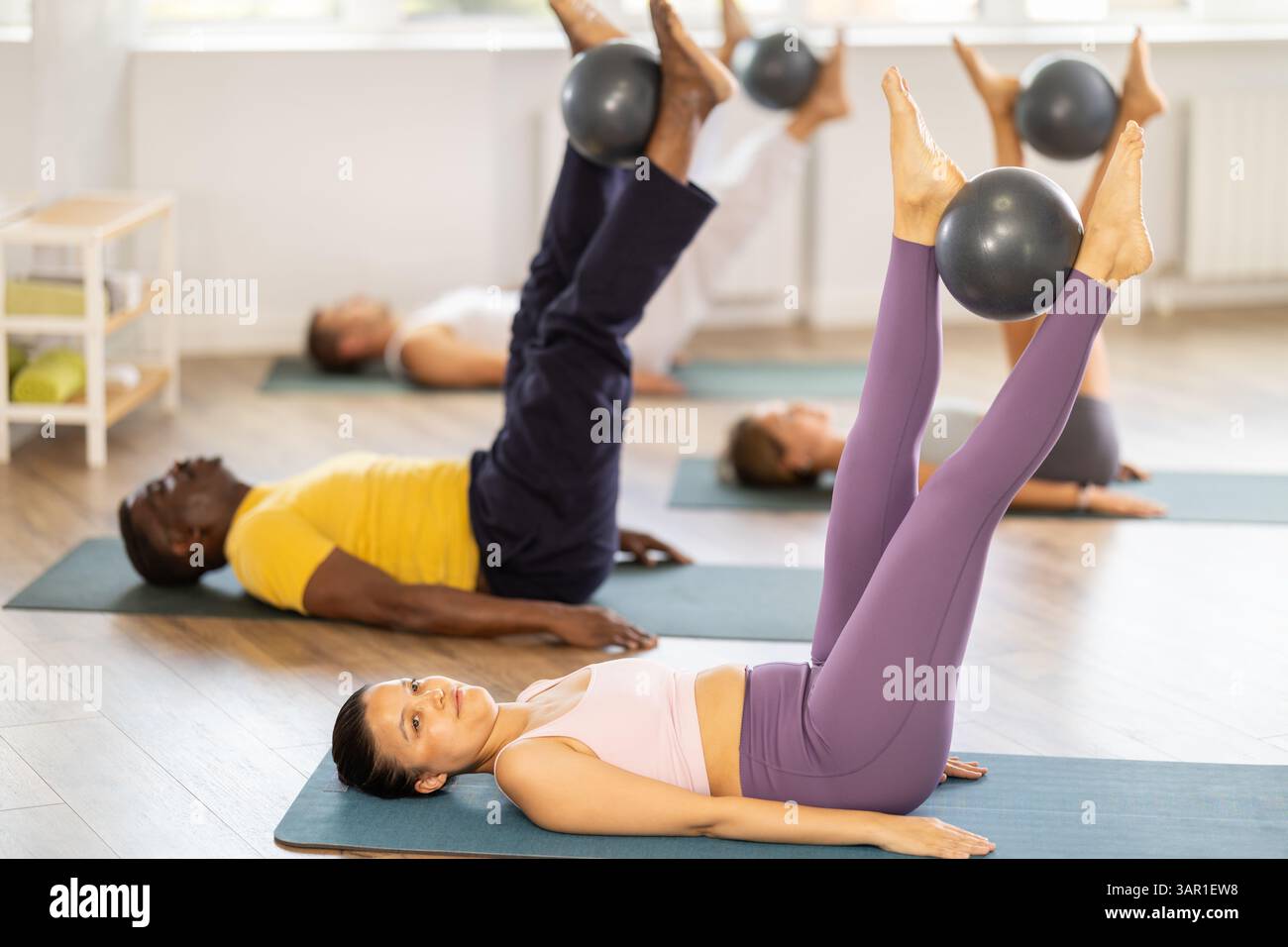 Asian woman doing Crescent Moon exercise with Pilates ball at group ...