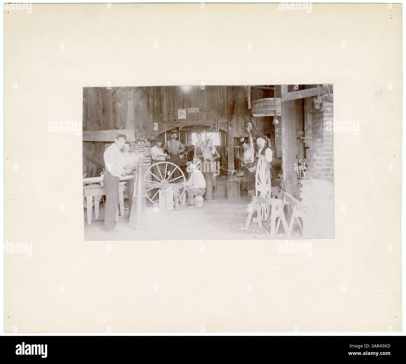 A black and white photograph of nine men in a blacksmith shop in the ...