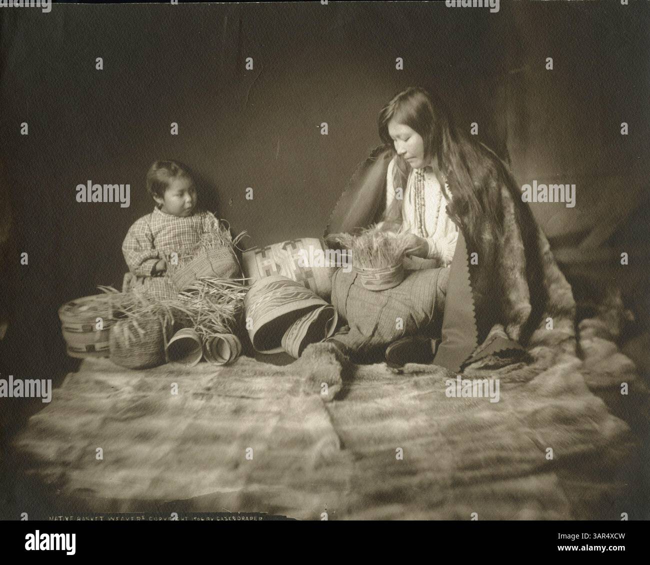 This photograph shows a Native American woman and child seated on a fur ...