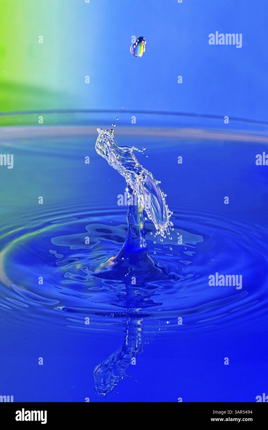 A single drop of water splashes in a blue liquid. The colours blue and ...