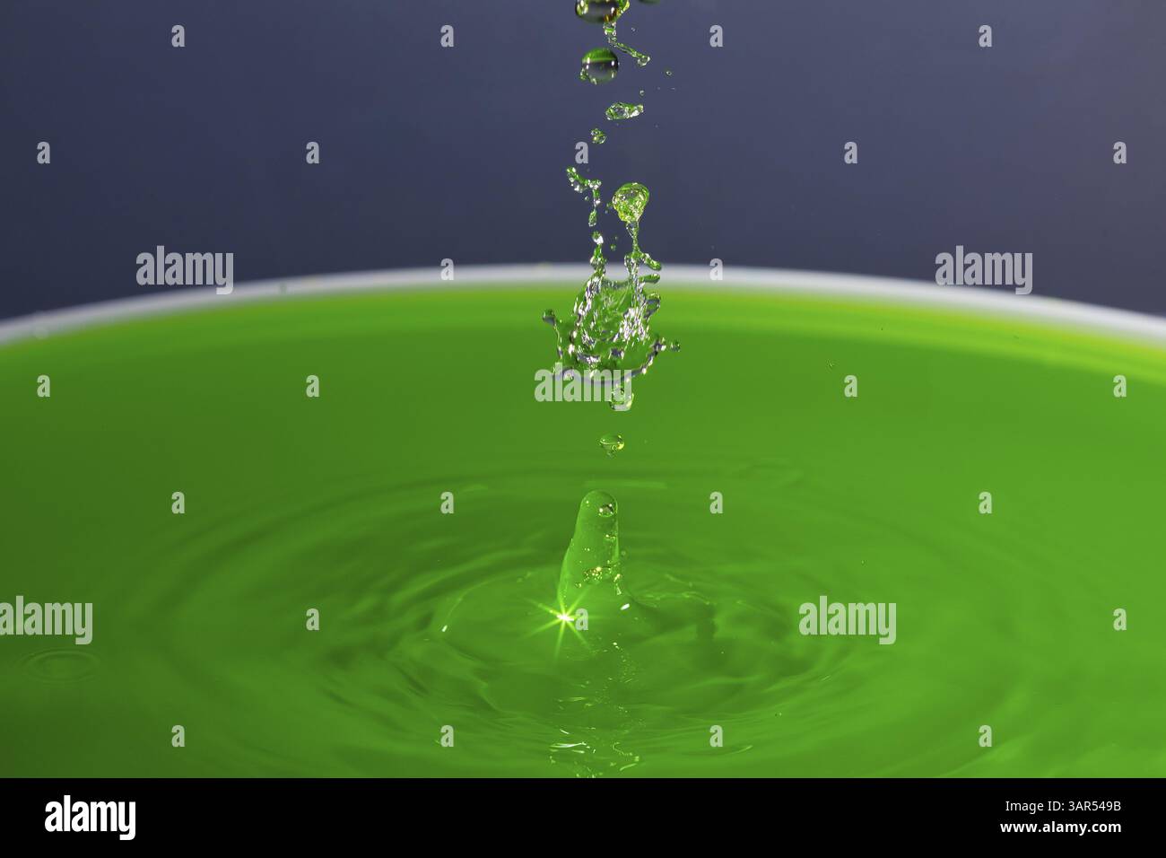 A green drop hits the water and causes a splashing reflection with a ...