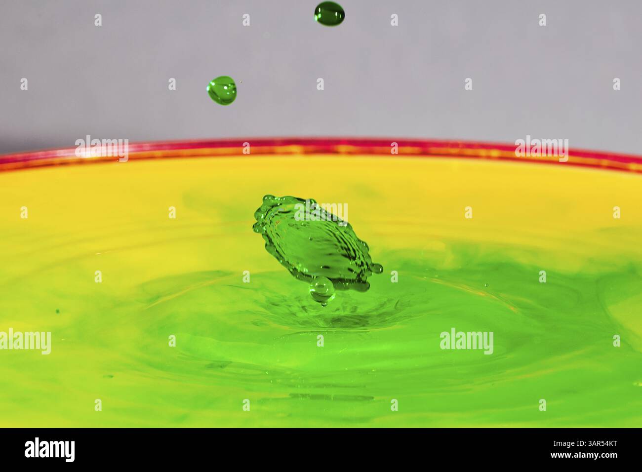 A green drop hits a yellow-green liquid and creates colourful patterns ...