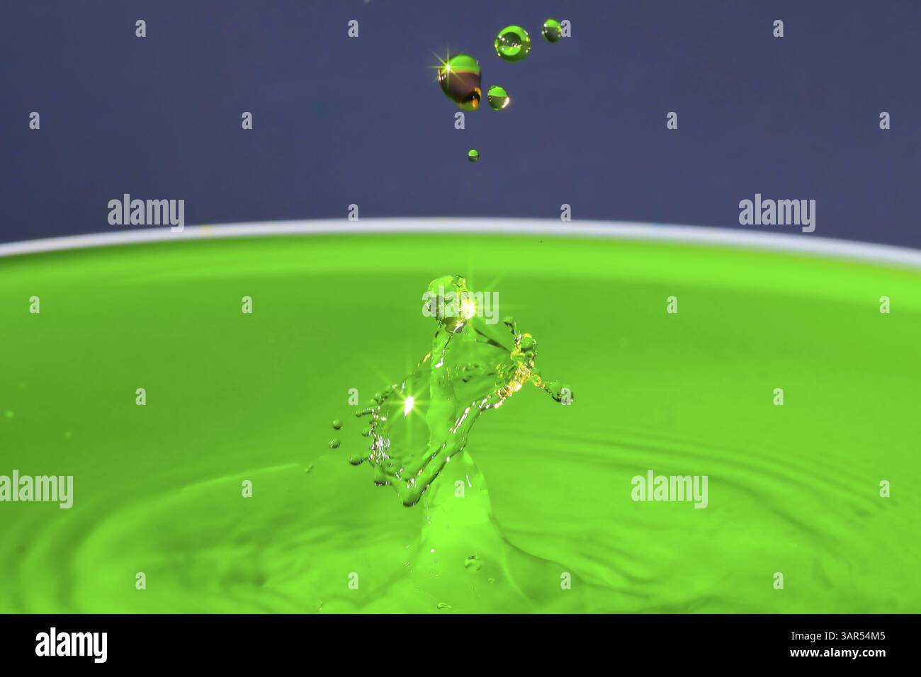 A green drop of water in dynamic motion, creating shiny splashes and ...