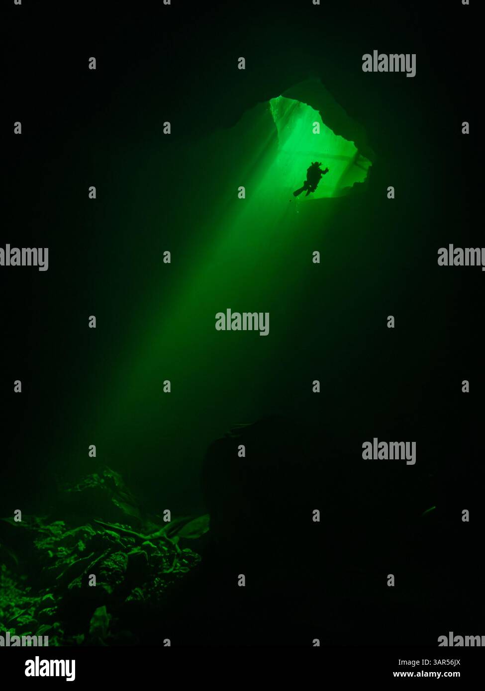 A single scuba diver caught in a beam of green light in the underwater ...