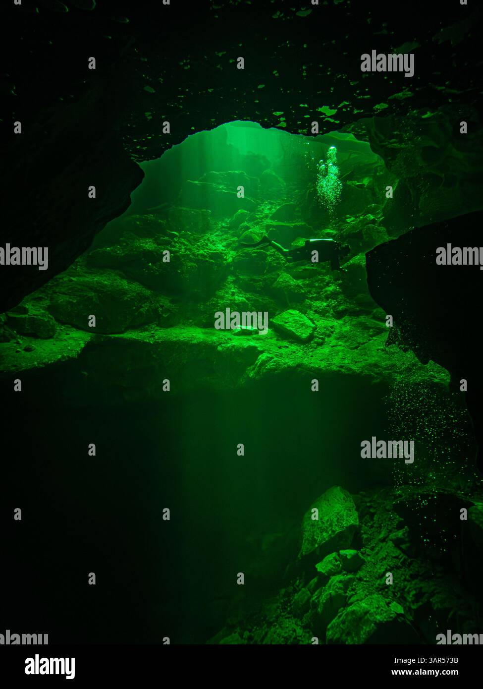 A single scuba diver caught in a beam of green light in the underwater ...