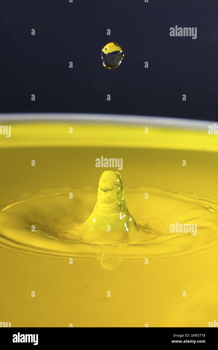Single yellow water drop falls on yellow surface in front of dark ...