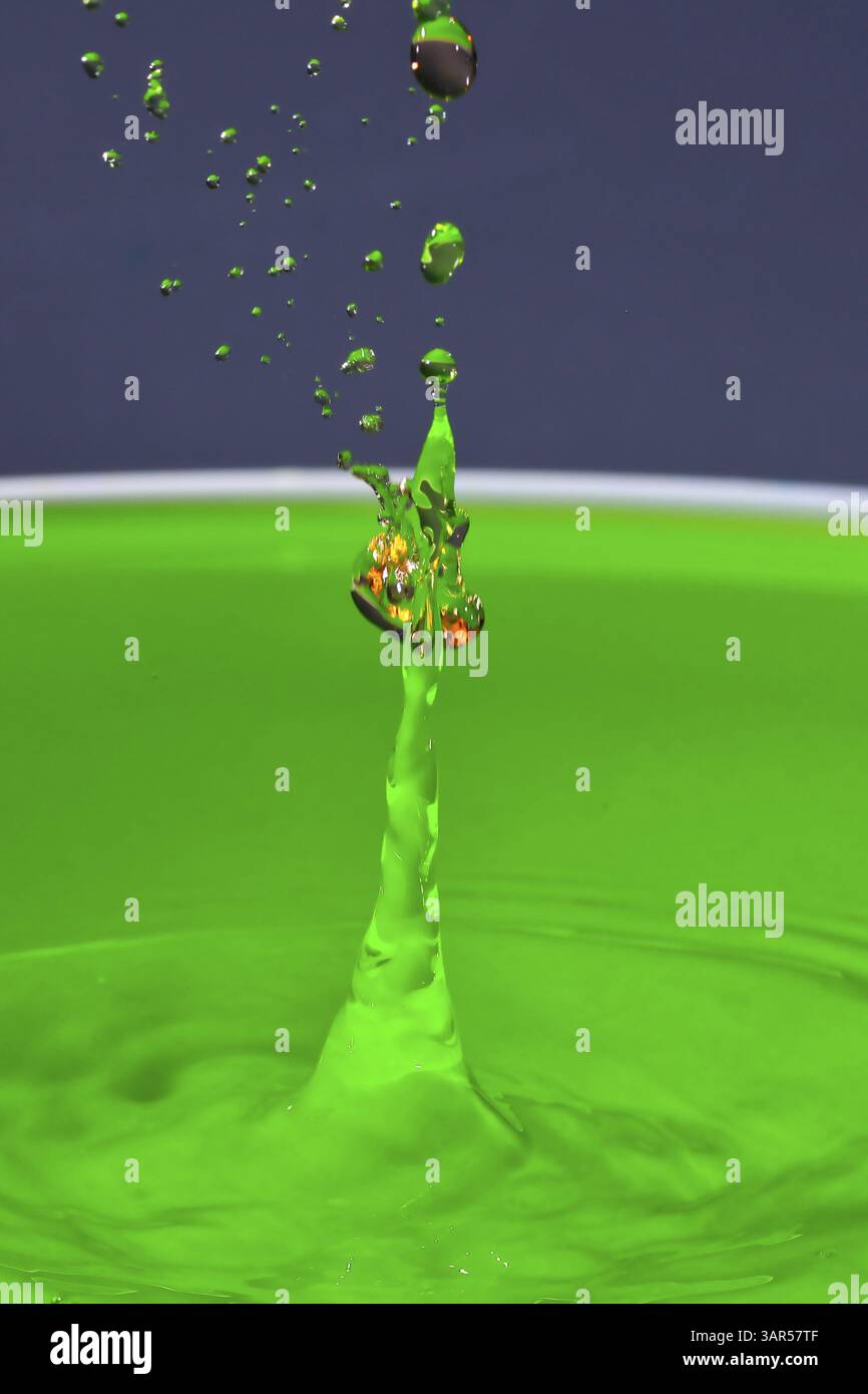 Green water drop falls on water surface in front of dark background ...