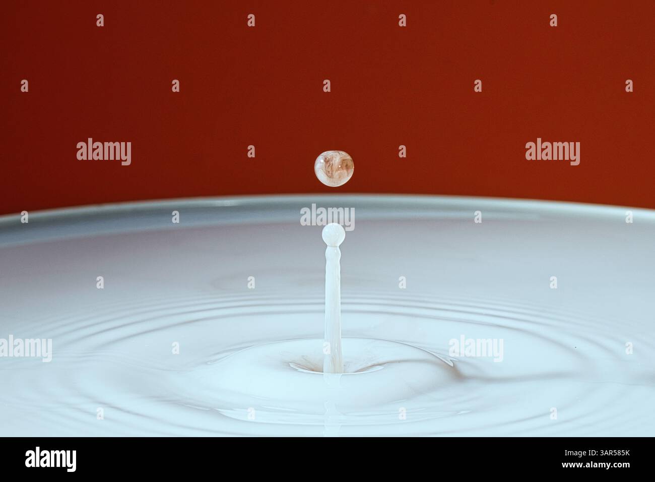 A drop floats over a wave of white liquid in front of an orange ...