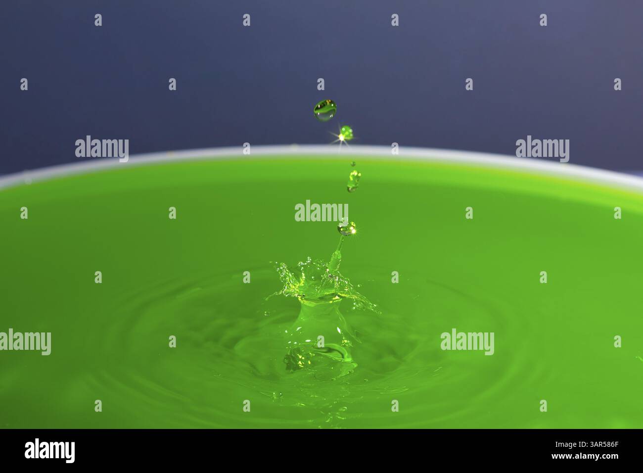 A water drop splashes with fine details into the air over a green ...