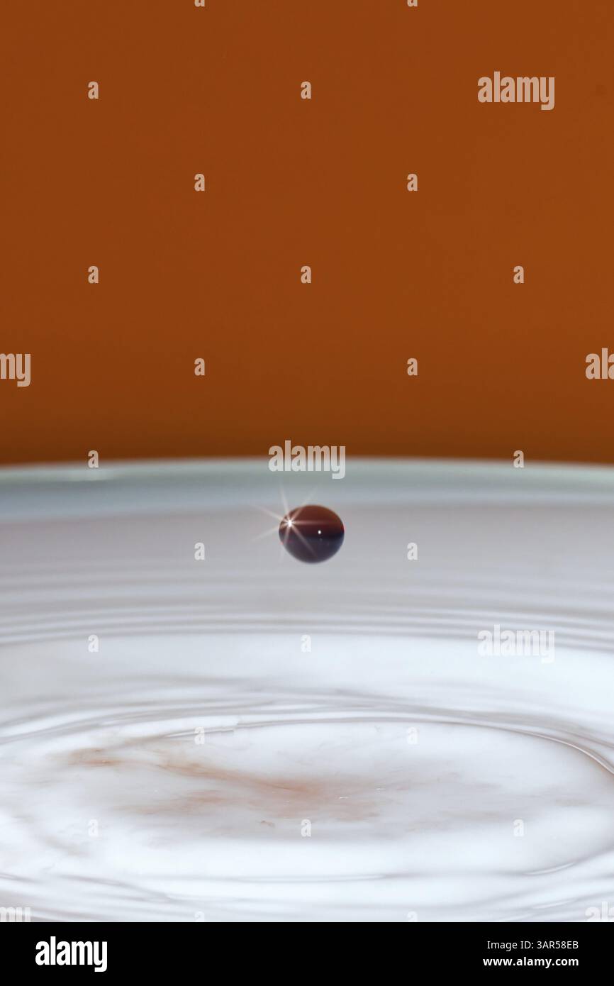 A single drop of water hits a water surface against an orange ...