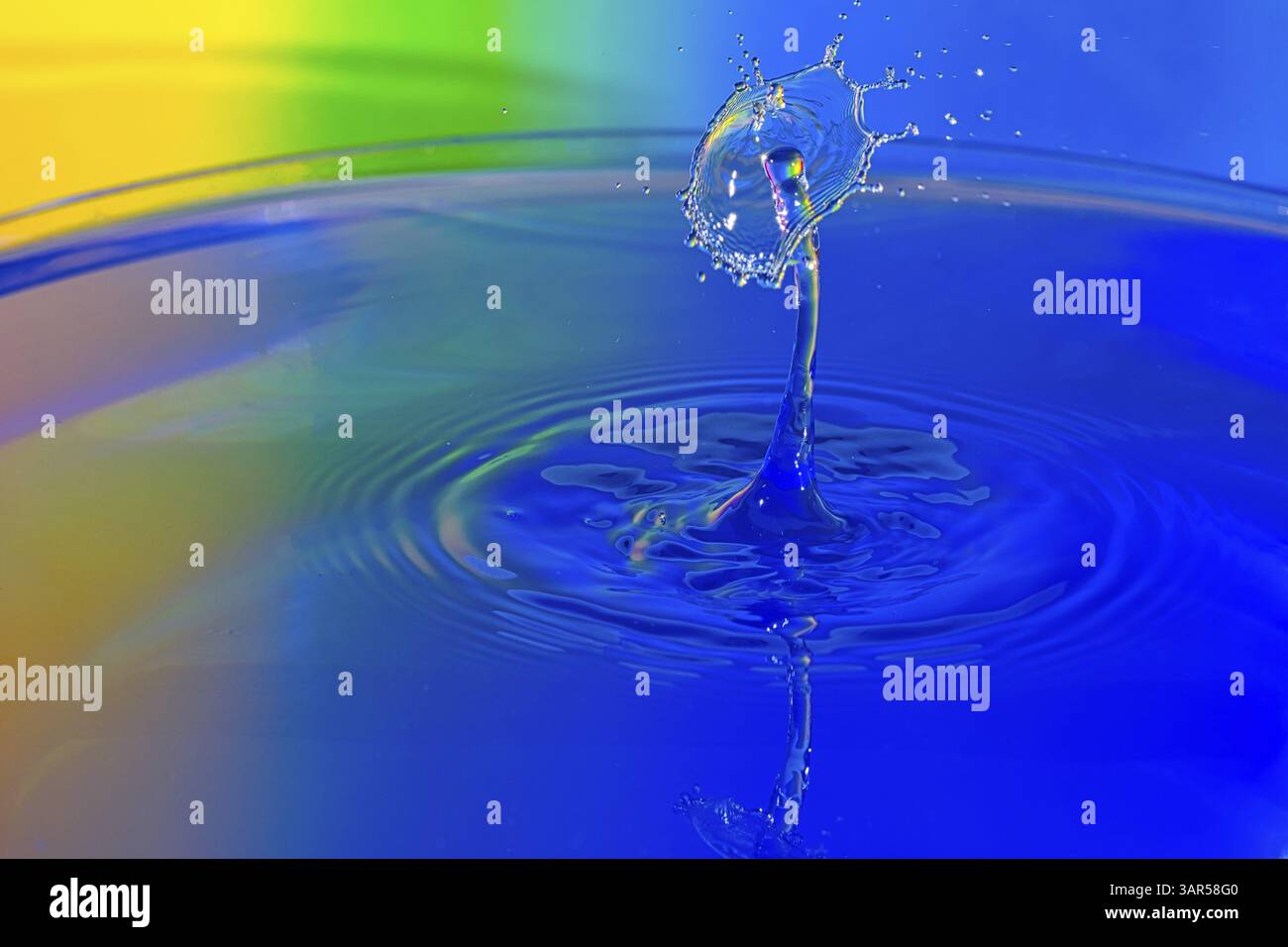 A drop of water creates splashes and waves in a colourful liquid with ...