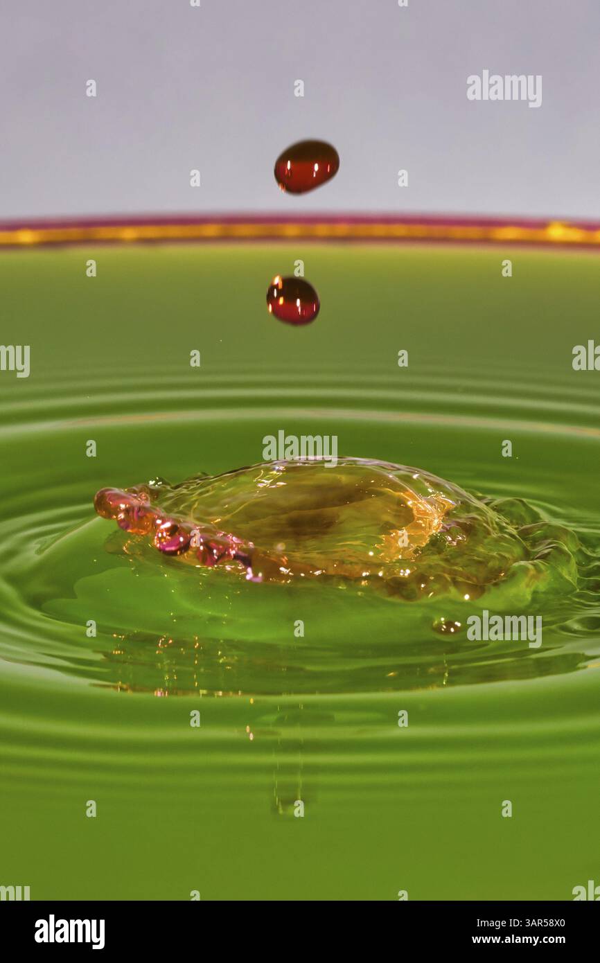 Coloured water drop falls and creates a splashing wave in green liquid ...