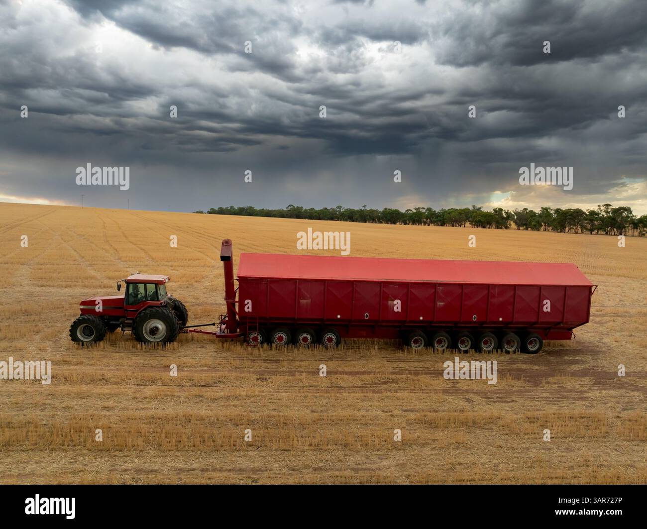 Aerial view of tractor towing a grain bin over dry farmland with rain ...