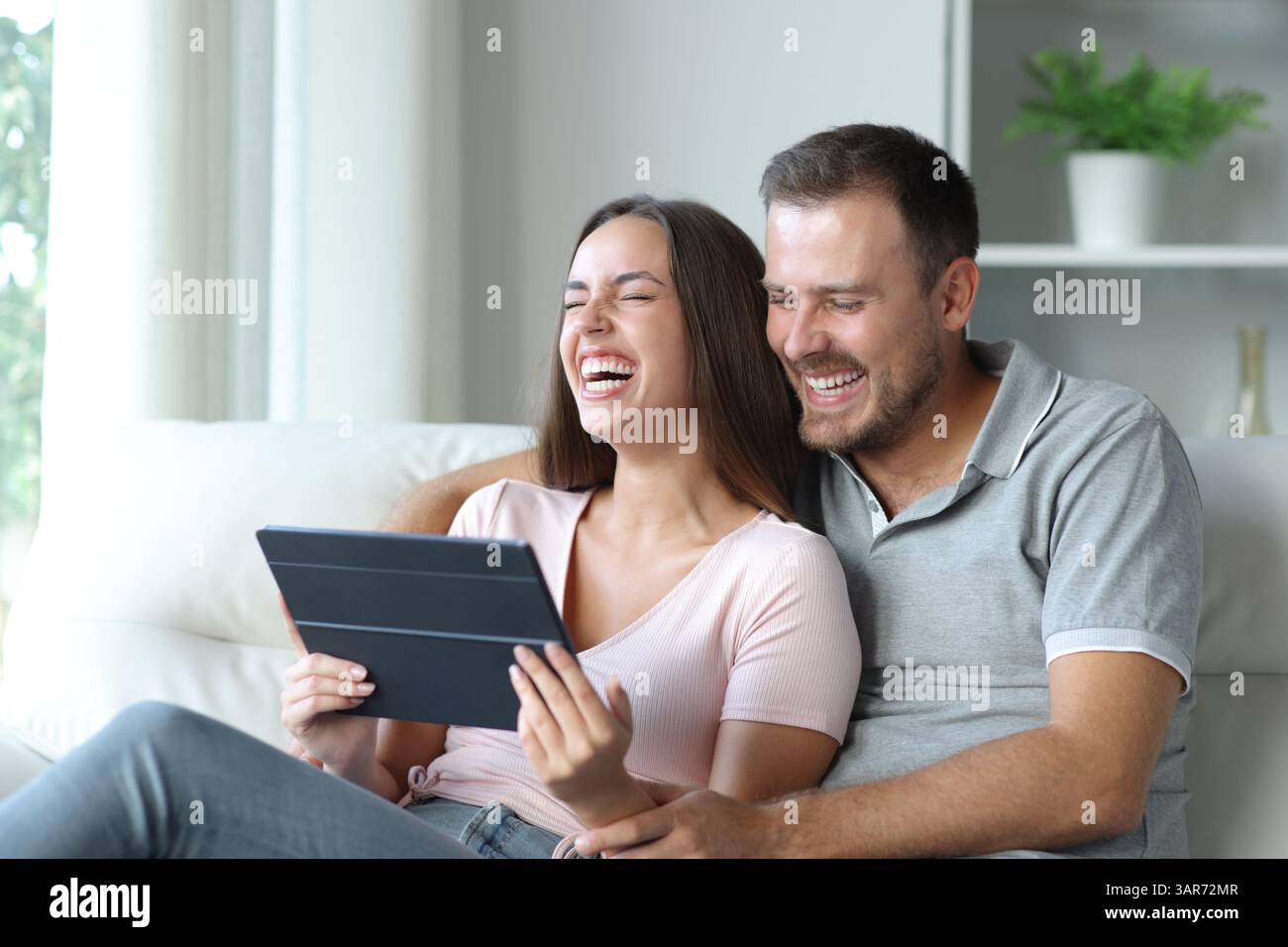 Funny couple watching media content on tablet and laughing loud sitting ...
