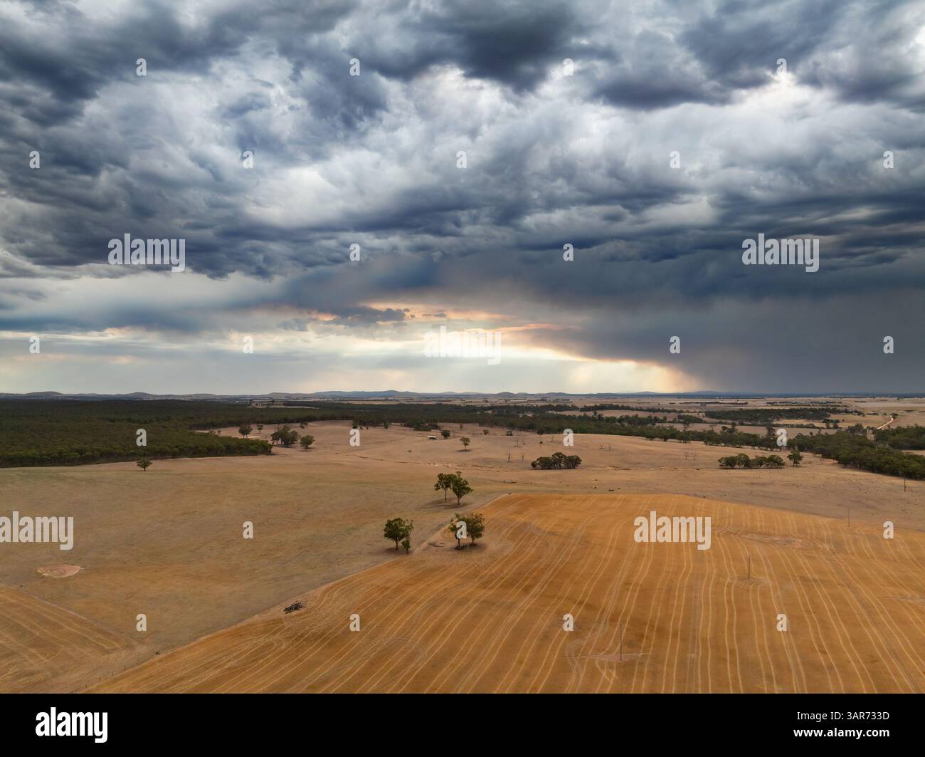 Aerial view of rain falling fron dark dramatic clouds over dry farmland ...