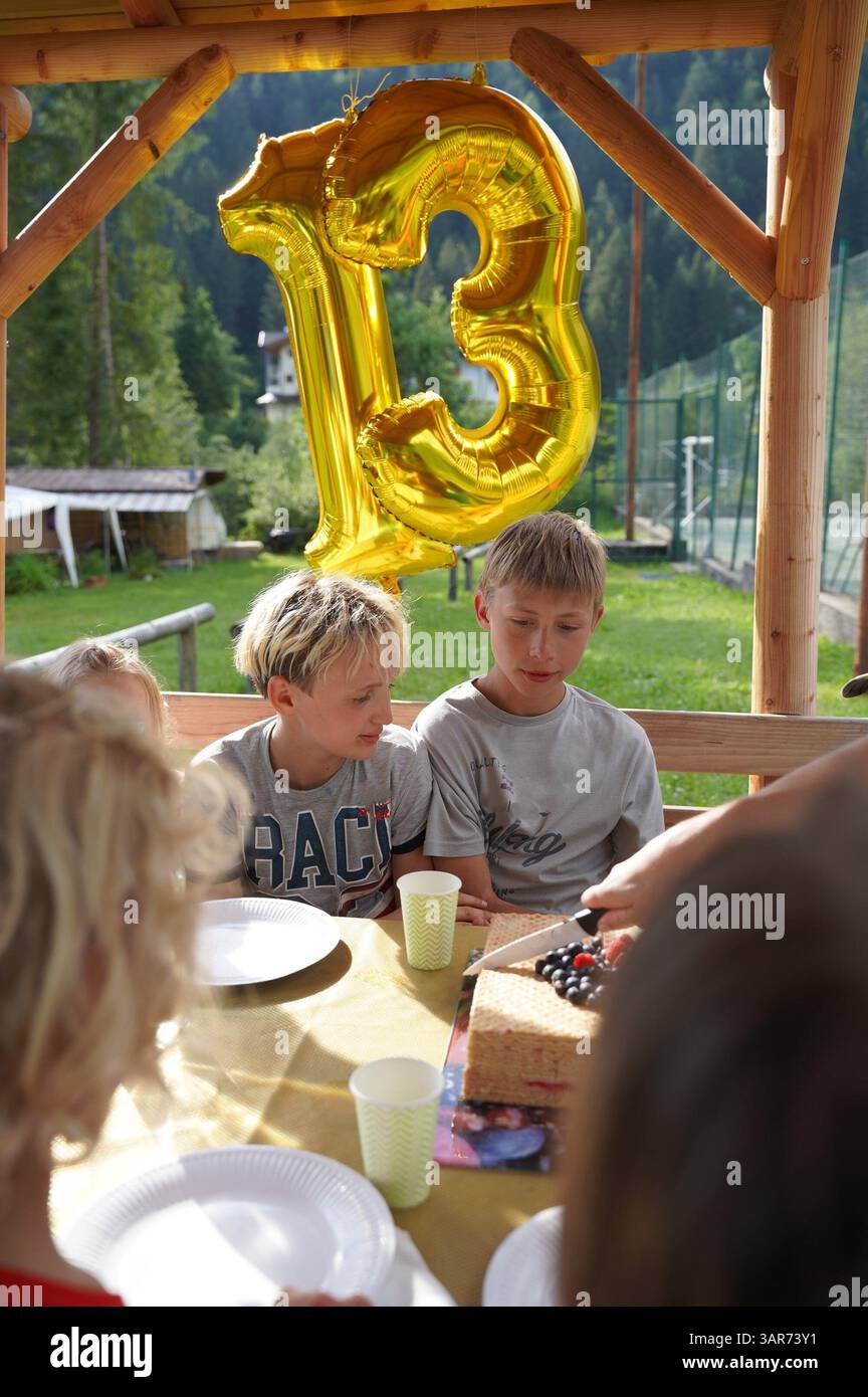 Group of children gathered around a table at an outdoor 13th birthday party. Positive ...