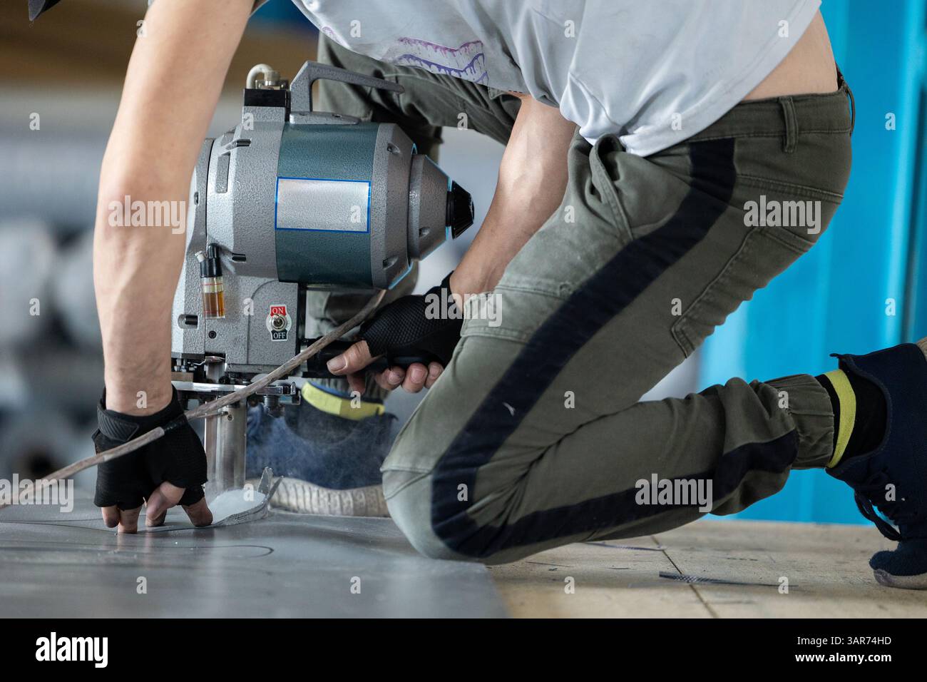 A worker wearing safety gloves uses an industrial reciprocating cutting ...
