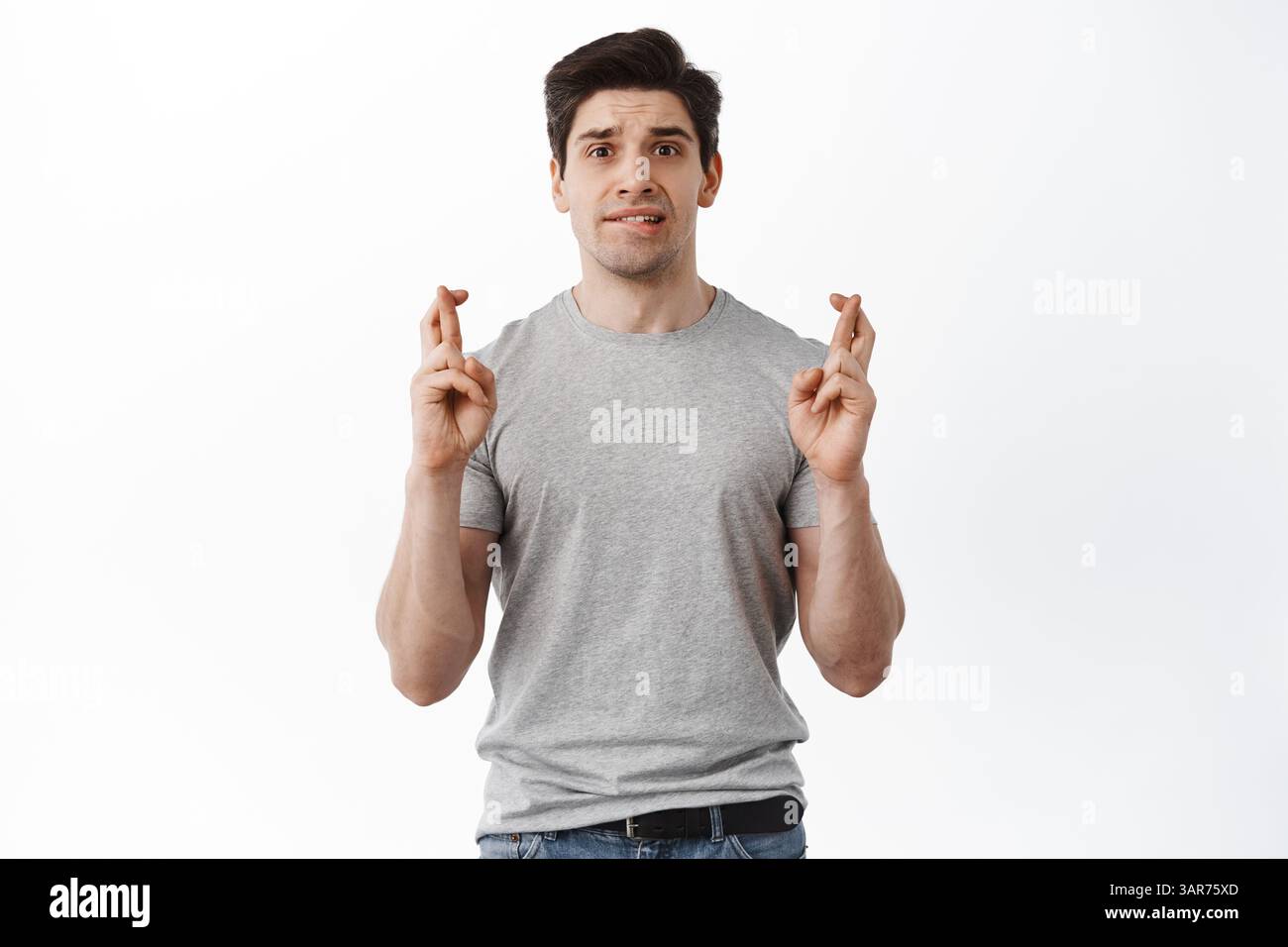Portrait of nervous guy cross fingers for luck, biting lip and frowning ...