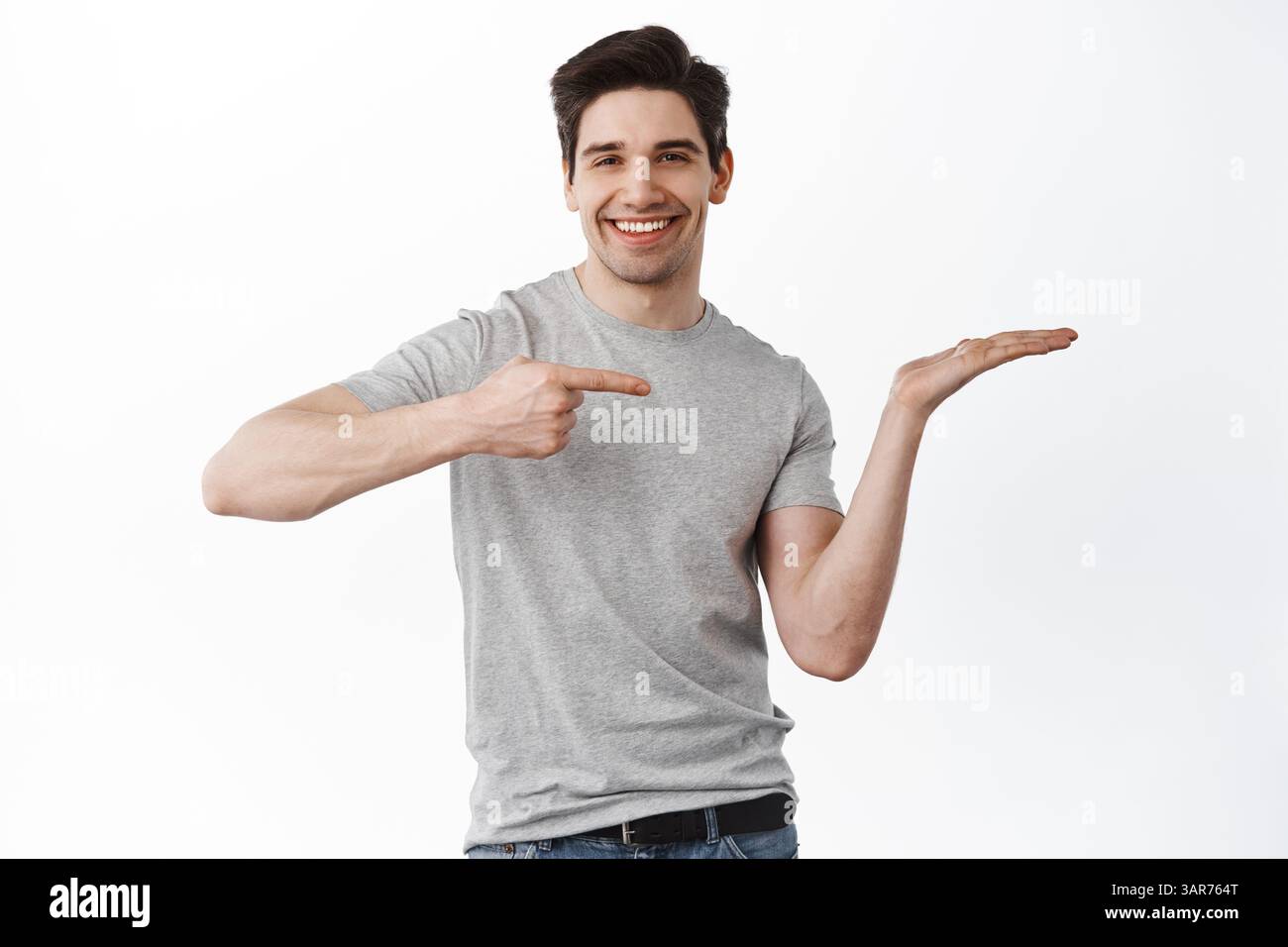 Image of handsome smiling man pointing at his empty hand, holding item ...