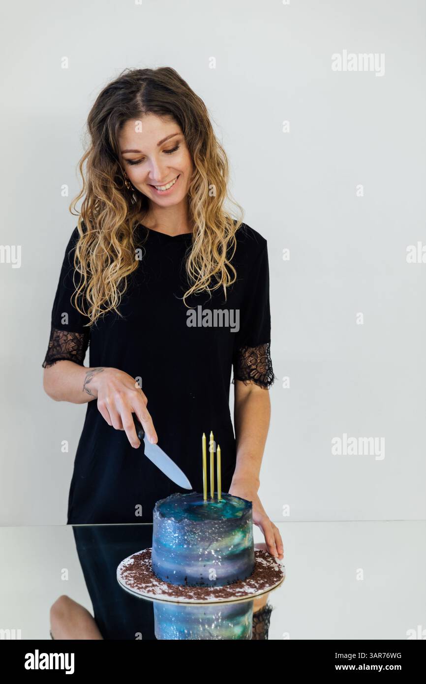 Beautiful woman cutting birthday cake and smiling Stock Photo - Alamy