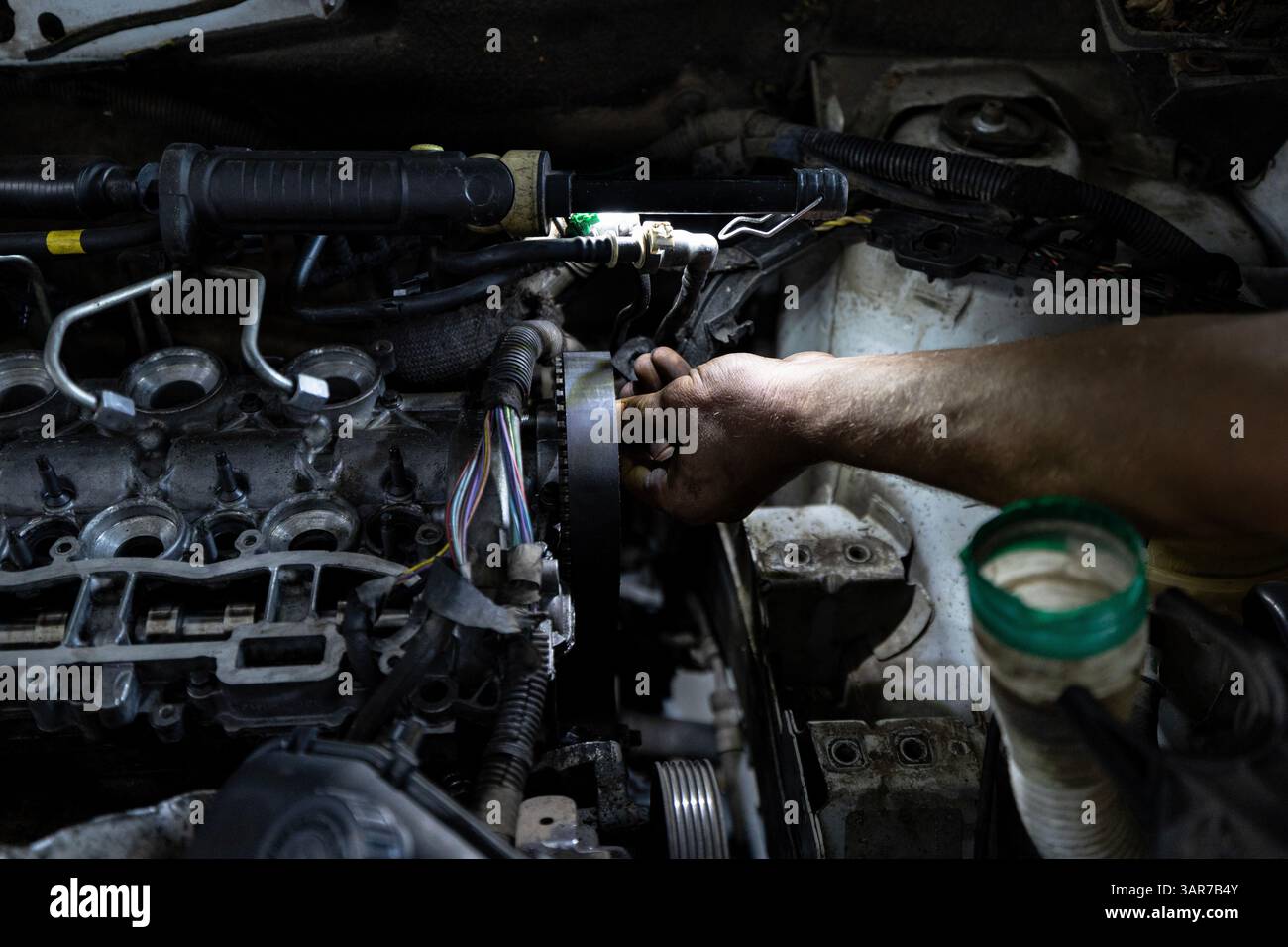 A mechanic's hand works on the timing belt area of a partially ...