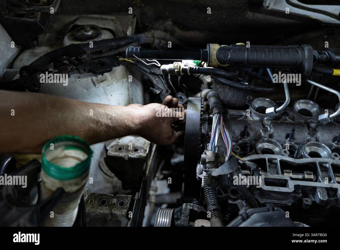 A mechanic's hand works on the timing belt area of a partially ...