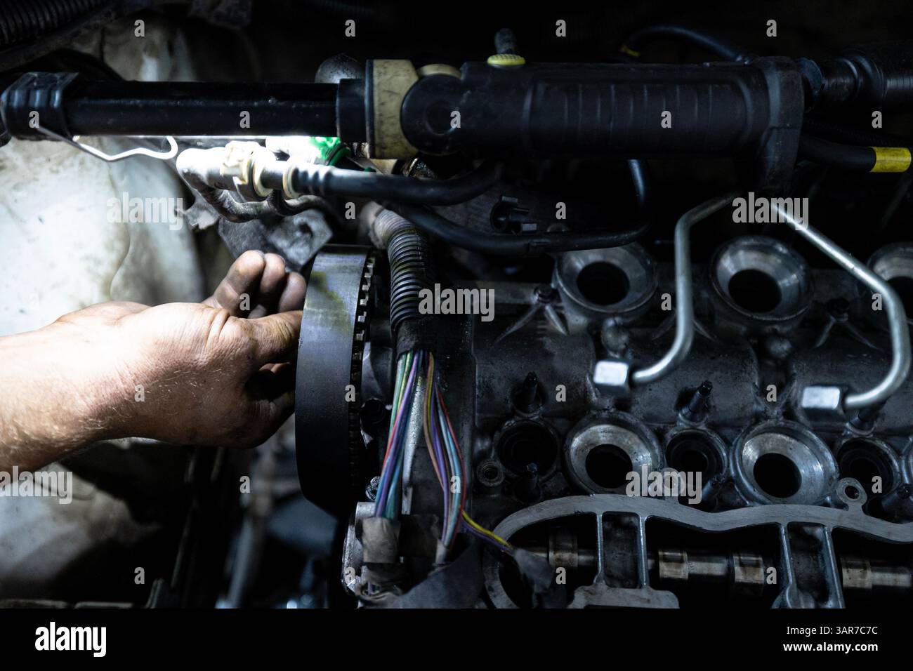 A mechanic's hand works on the timing belt area of a partially ...