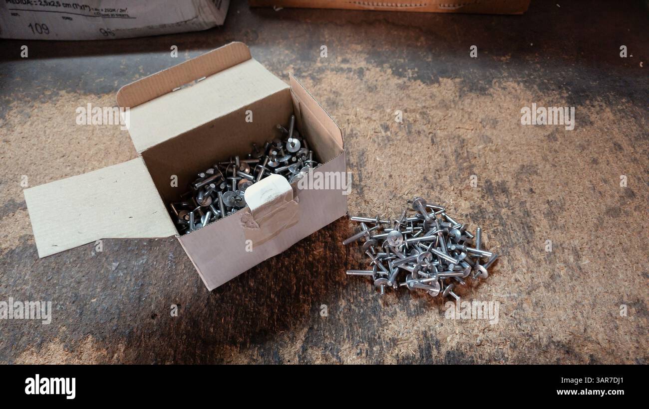 Blind rivets spilling from an open cardboard box onto a sawdust-covered ...