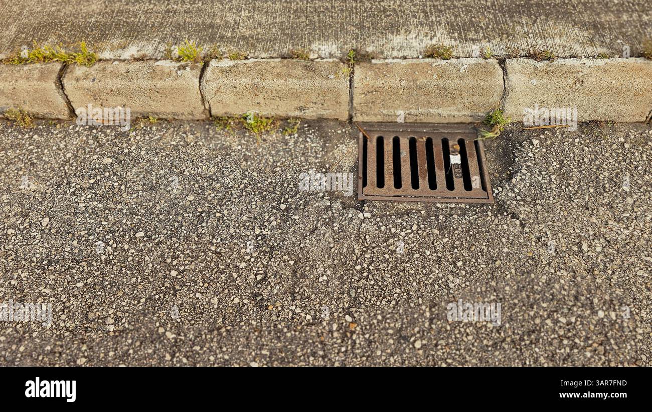 Close-up of a sewer grate draining water on an asphalt road next to a ...