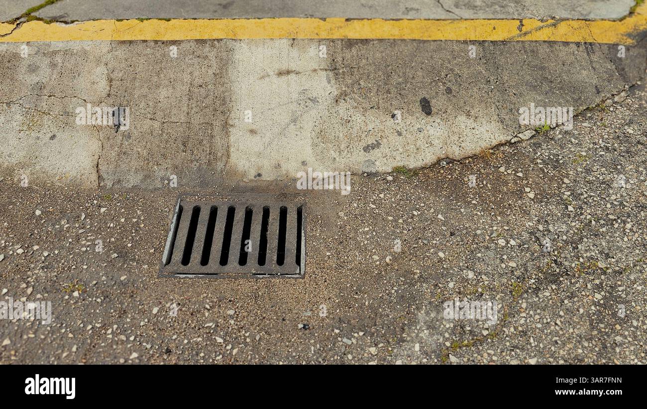 Metal storm drain grating embedded in asphalt next to a concrete curb ...