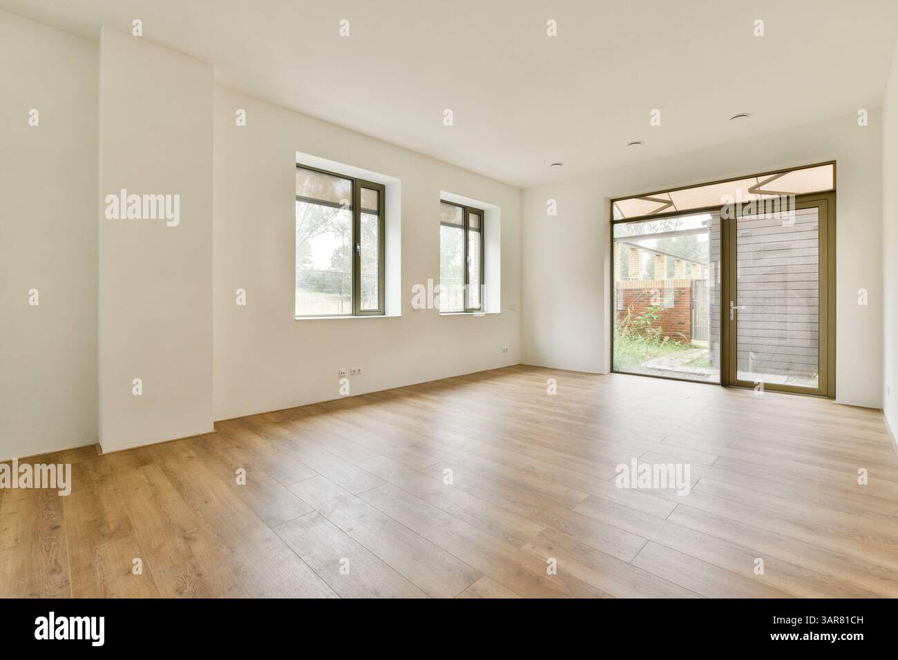 An empty, well-lit room with large windows and wooden flooring ...