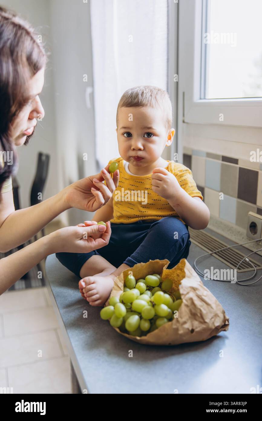 Mother feeding her baby fresh grapes from an eco-friendly paper bag ...