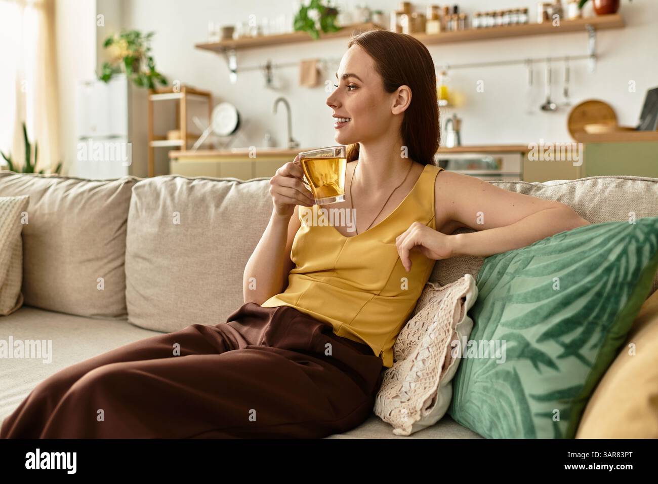 A young beautiful woman sips tea while relaxing comfortably on her ...